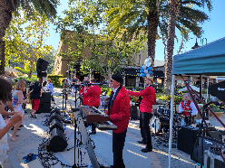Band in red coats performing in plaza with storefront and palm trees in ...